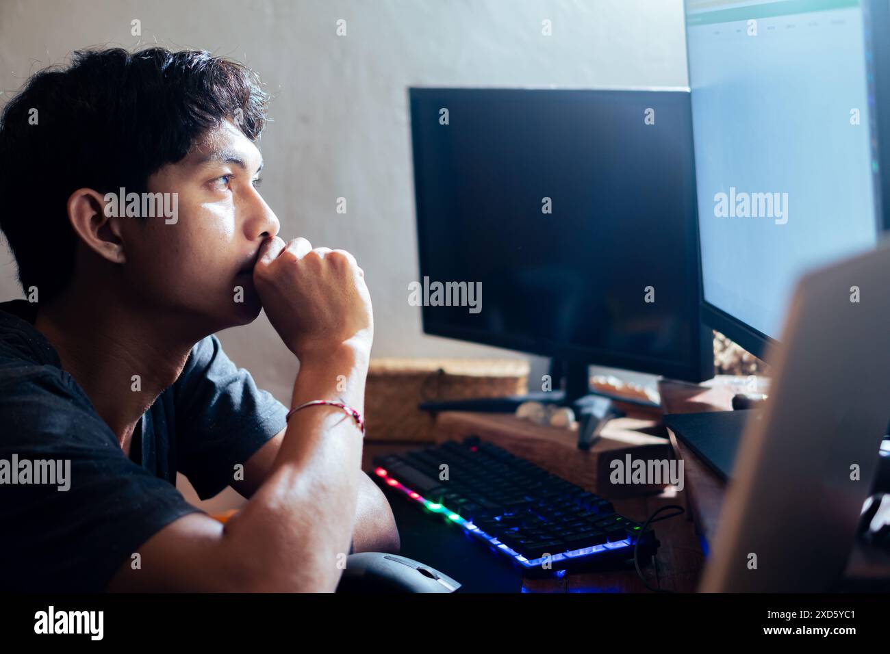 A young man sitting at a desk, looking intently at a computer screen. He appears to be deep in ...
