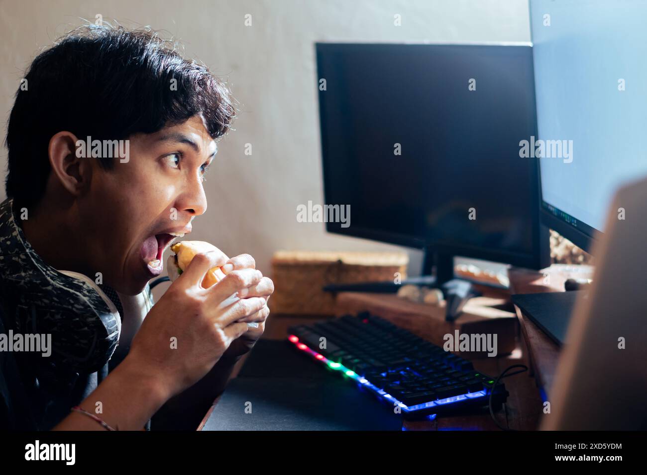 A person enthusiastically eating a sandwich while sitting at a computer ...