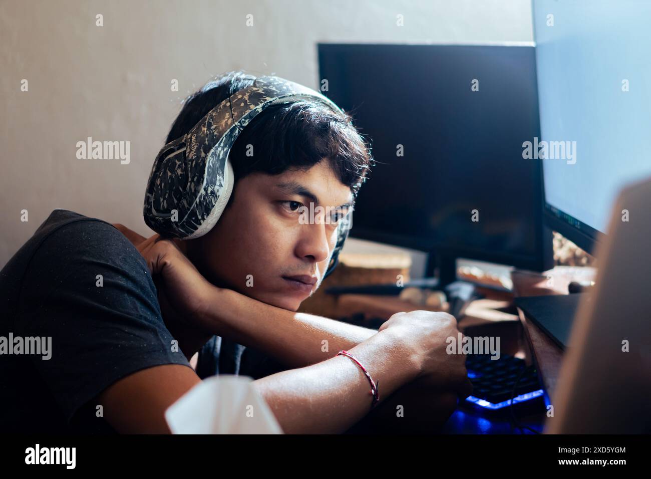 A young man wearing headphones is sitting at a desk, staring intently ...