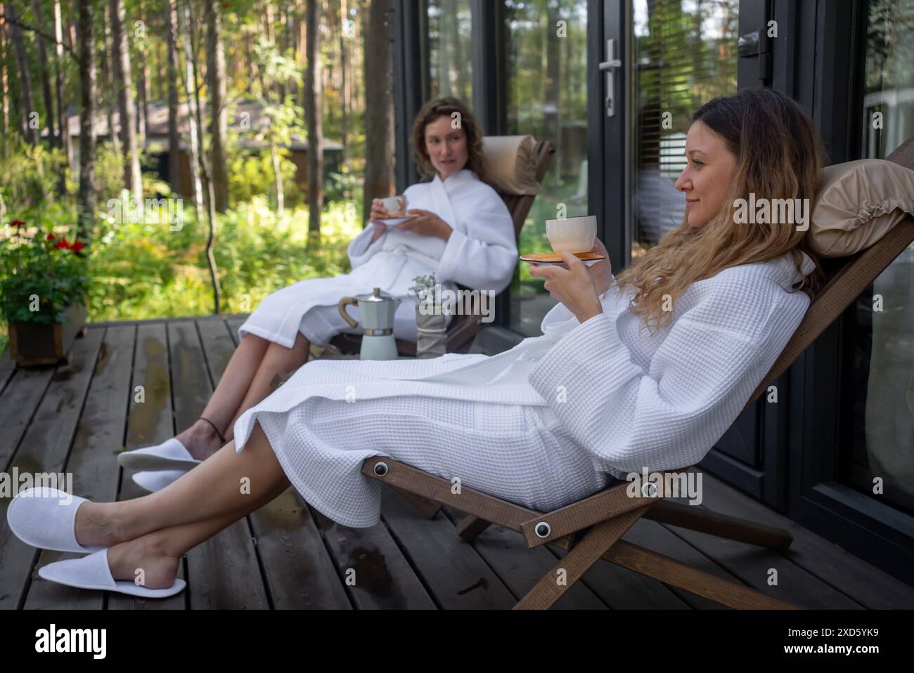 Two women in white robes lounging on deck with coffee, surrounded by ...
