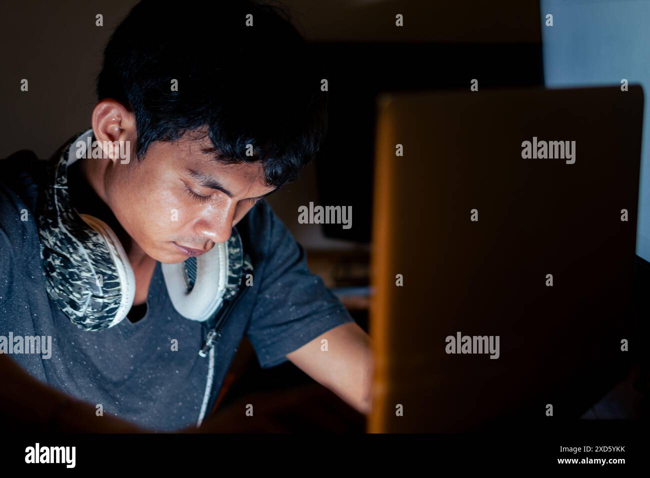 Young man focused on working on a laptop with headphones around his ...