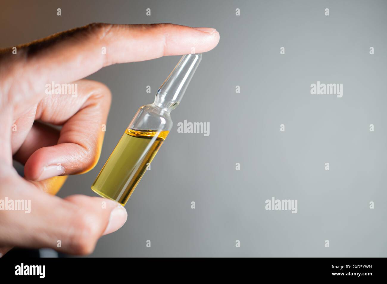 A hand holding a small glass vial containing a yellow liquid against a ...