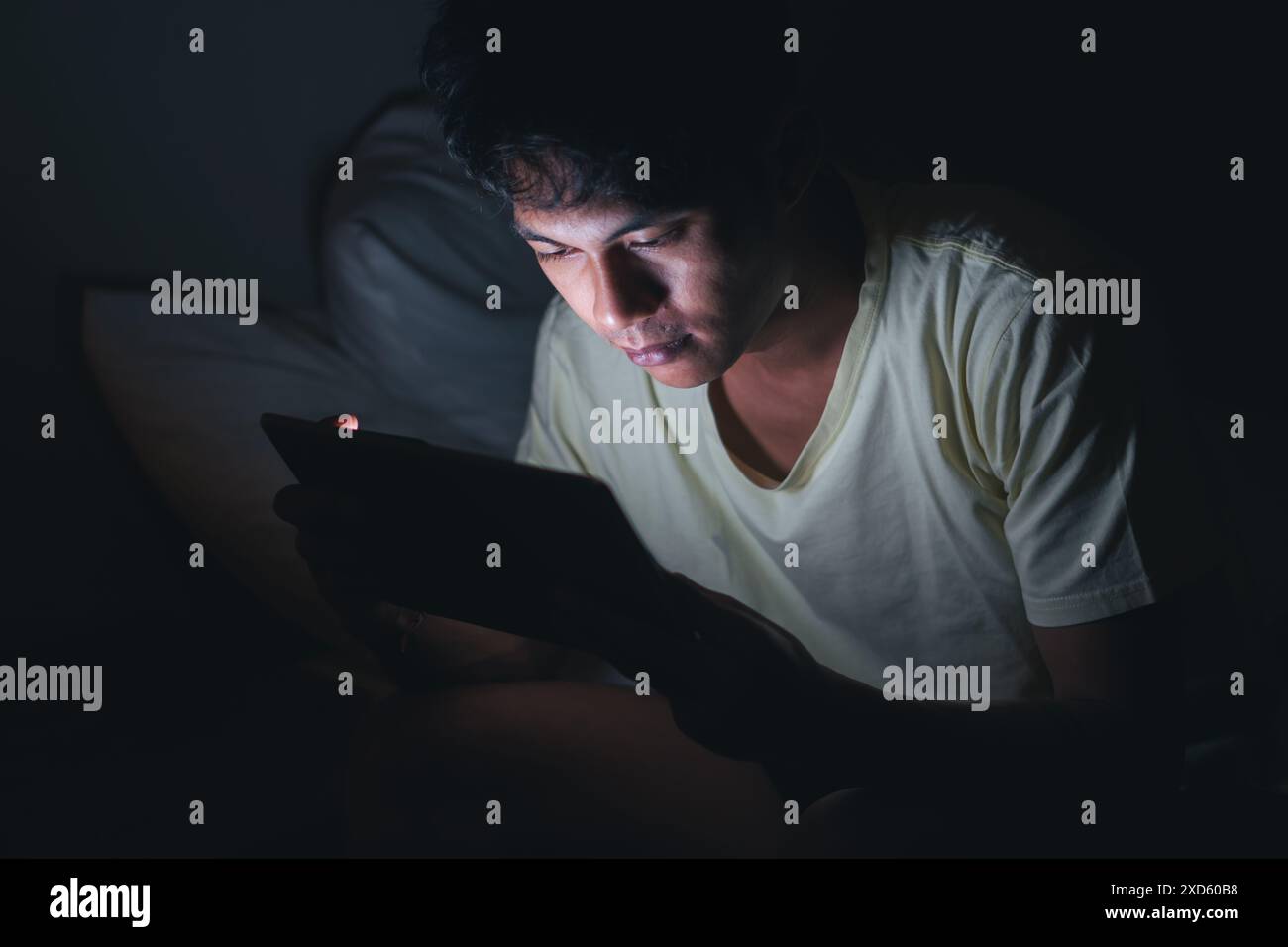 A man in a dimly lit room looking at a tablet screen, with the light ...
