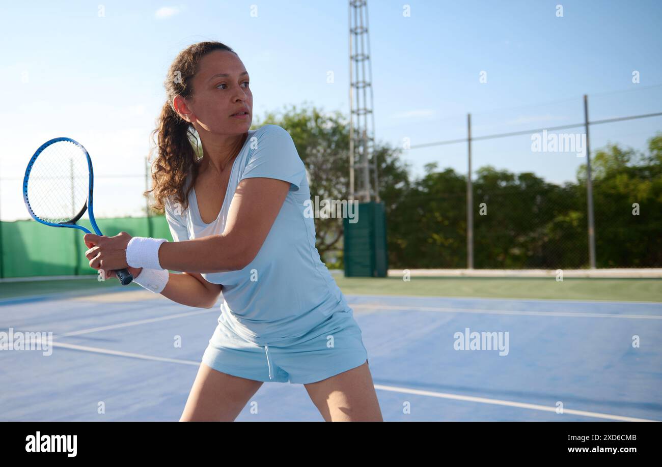 A woman in athletic attire playing tennis on an outdoor court. She ...