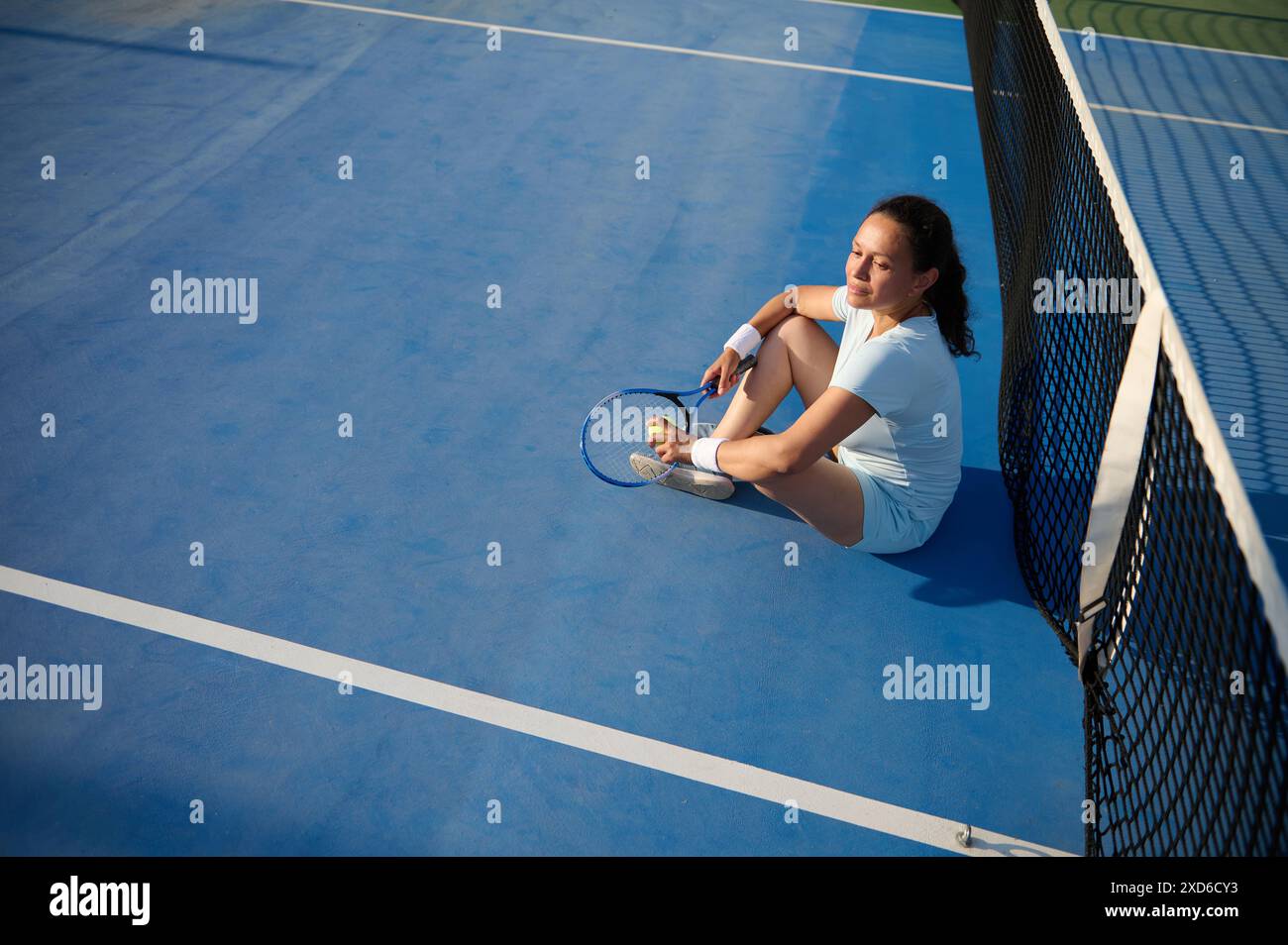 Woman in sportswear sitting on a blue tennis court, resting after a ...