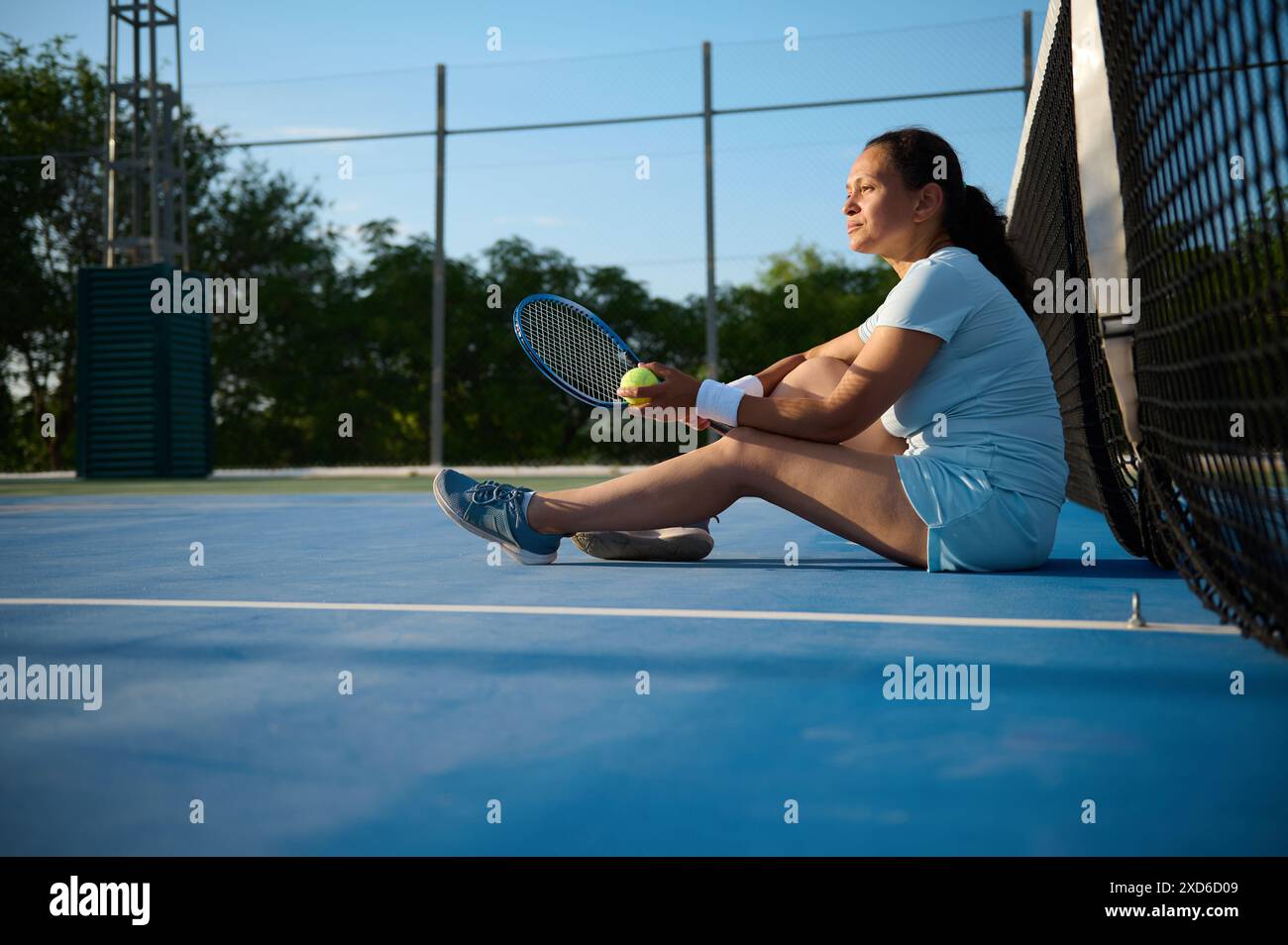 Female tennis player sitting by the net, taking a break on an outdoor ...