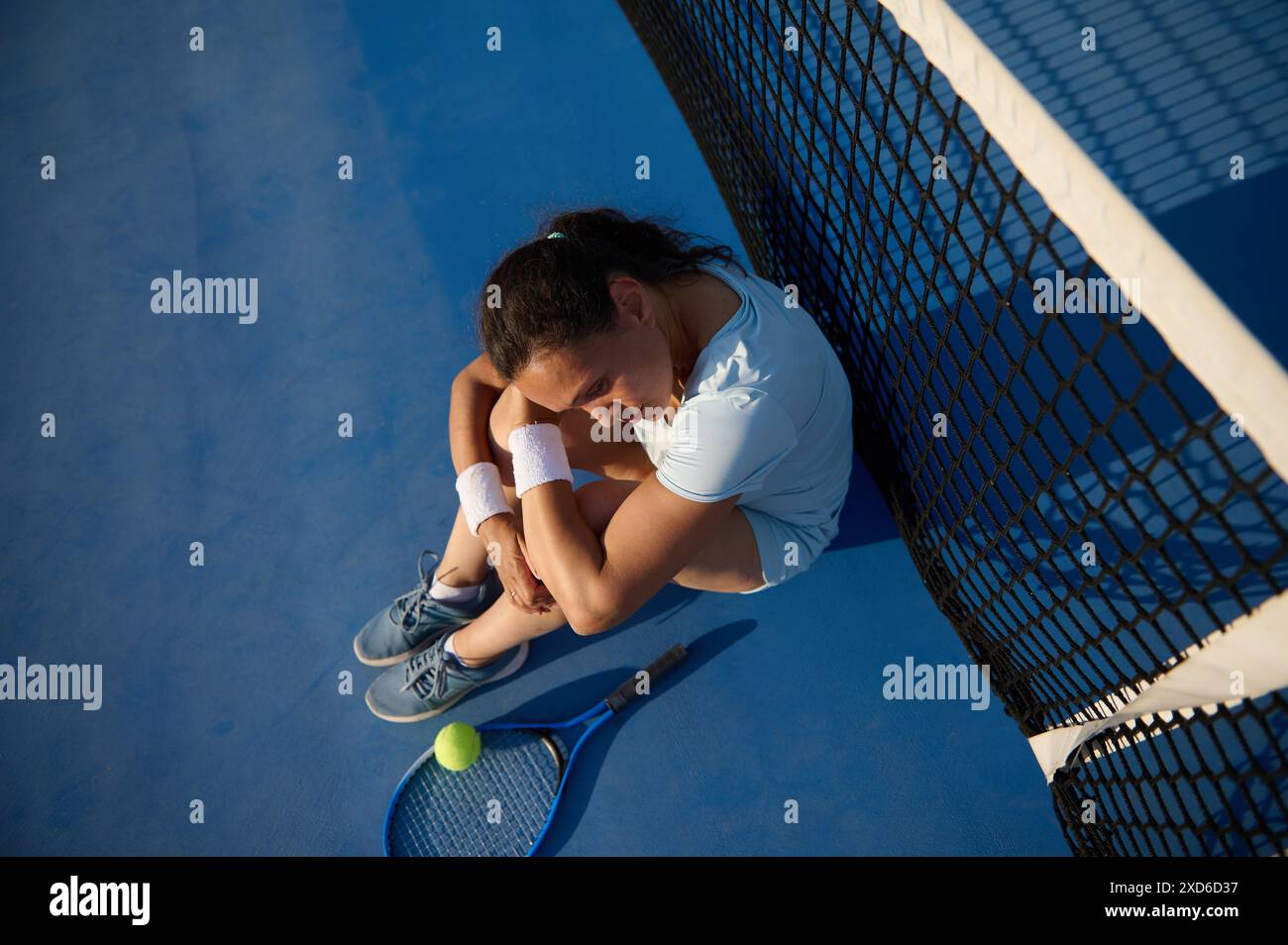 Overhead view of a tired female tennis player sitting on a blue court ...