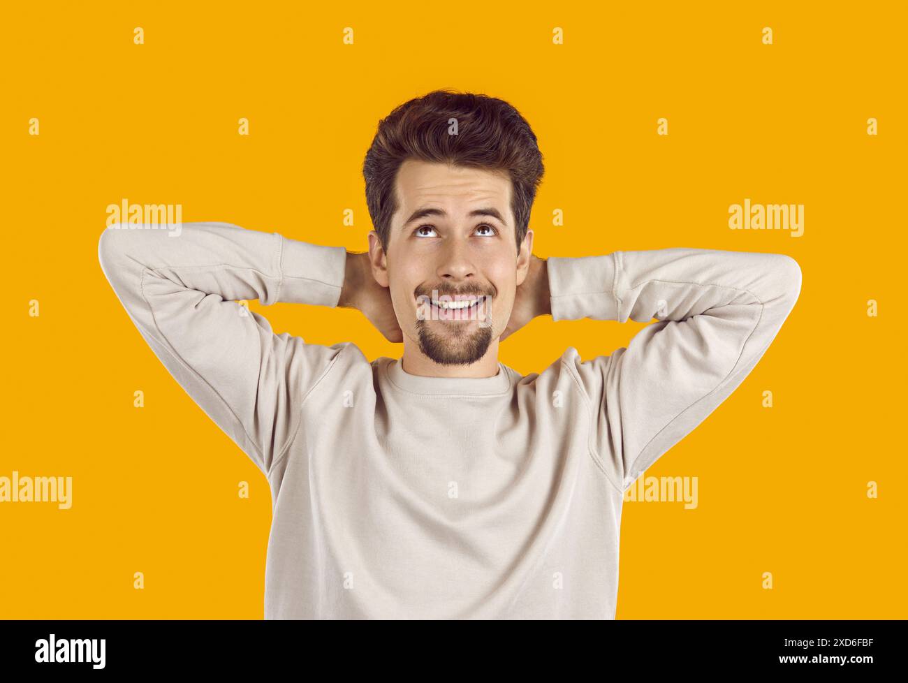 Happy young man holding his hands behind his head, looking up, thinking ...