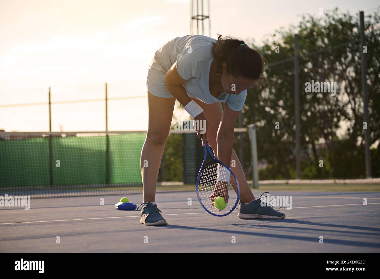 A female tennis player bending down to pick up a ball on an outdoor ...