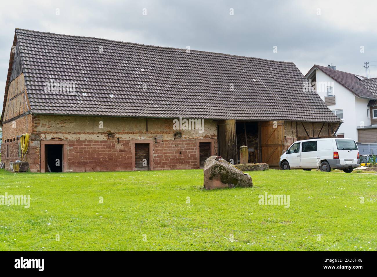 A white van is parked in front of a red barn on a grassy field. The ...