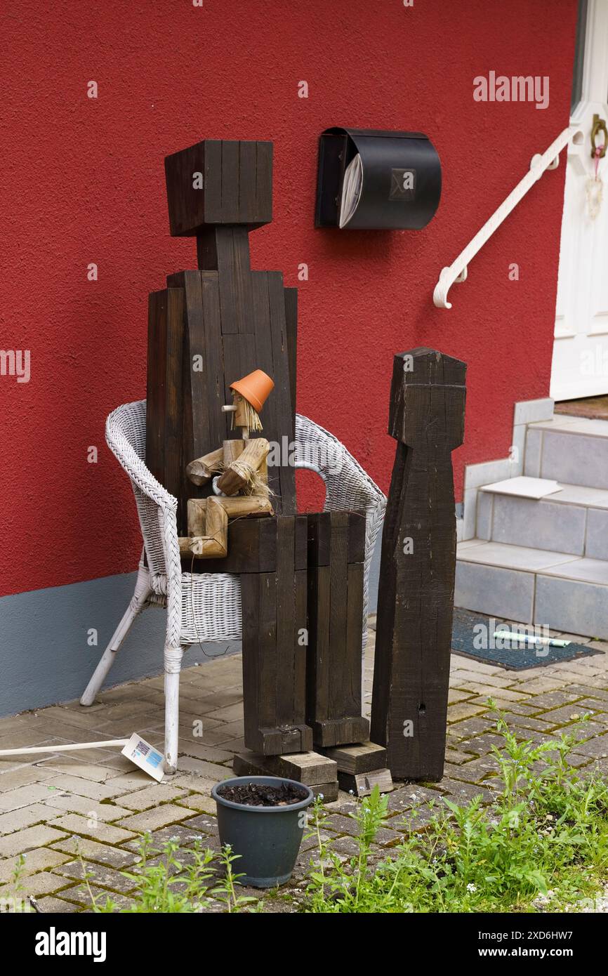A dark brown wood sculpture of two figures on a white chair outside a ...