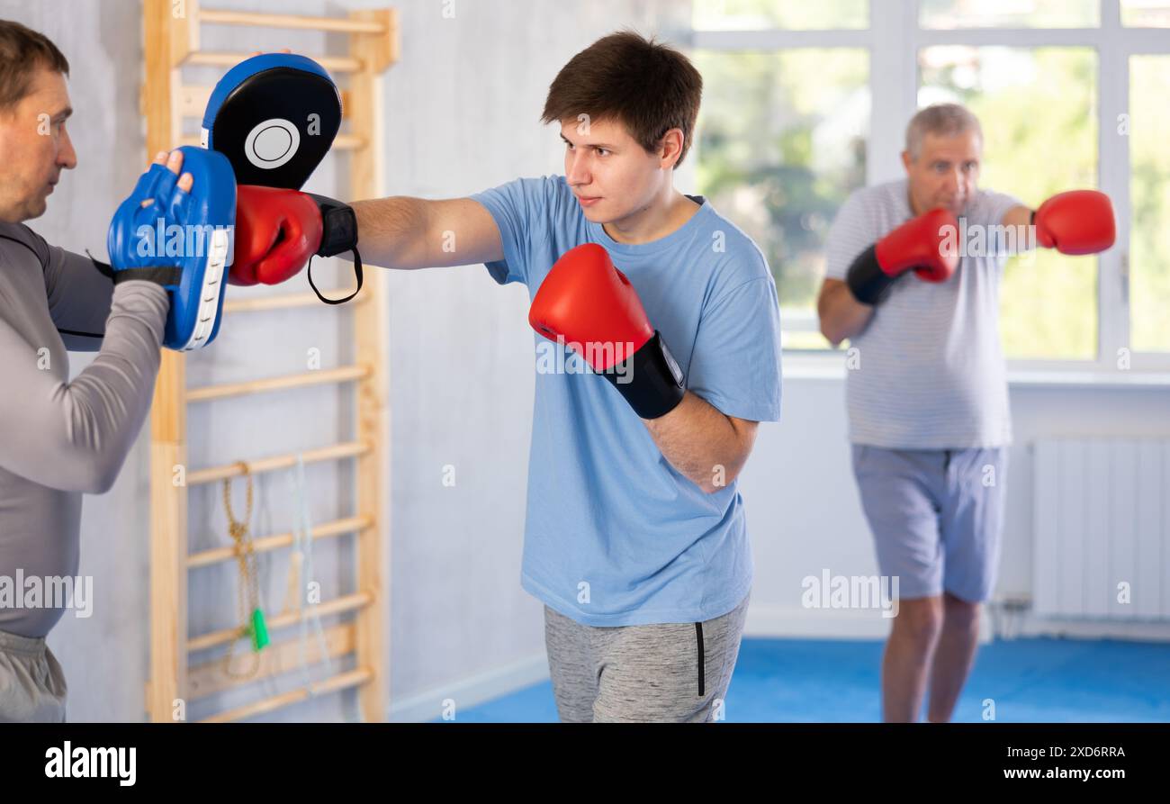 Guy in boxing gloves practicing punches on mitts with coach during self ...