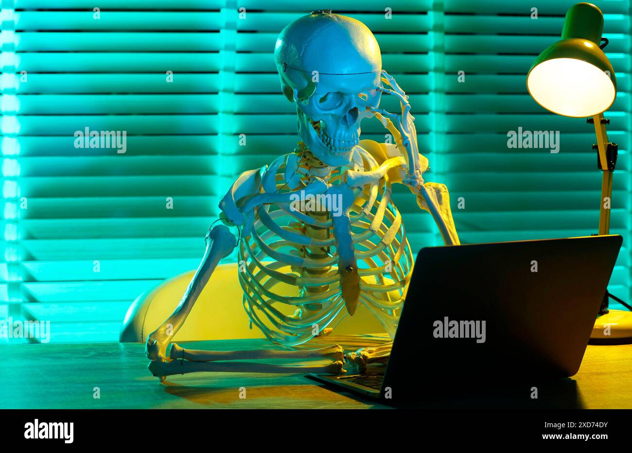 Waiting concept. Human skeleton sitting at wooden table with laptop ...