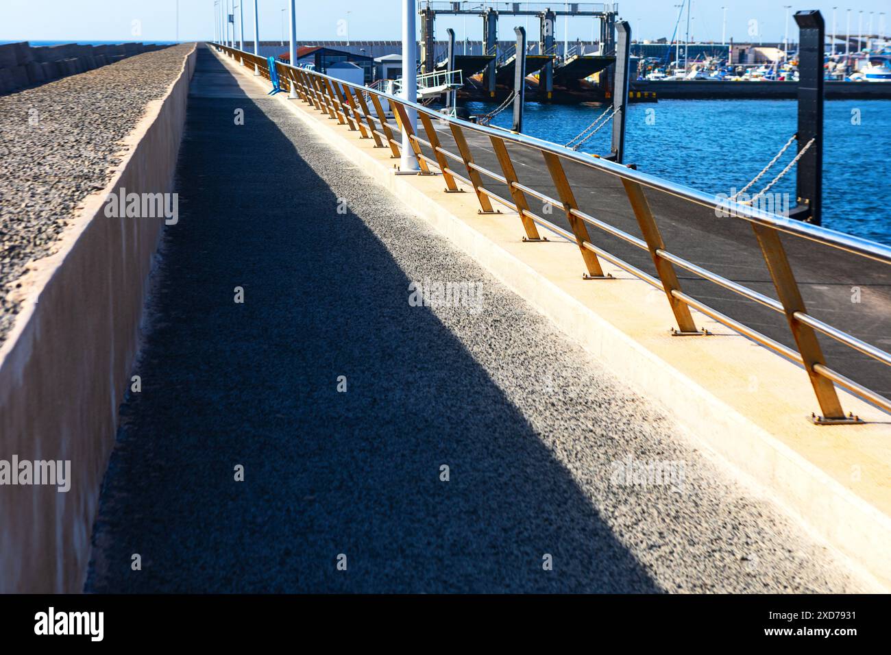 A long walkway with a railing and a dock in the background. The walkway ...