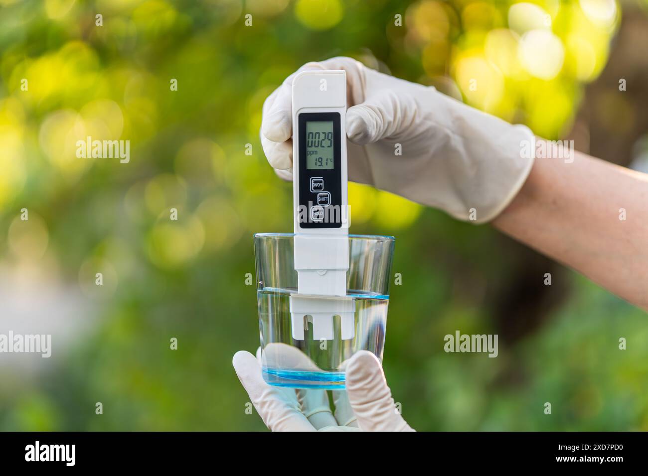pH meter in hands with gloves, glass of water on blurred background of ...