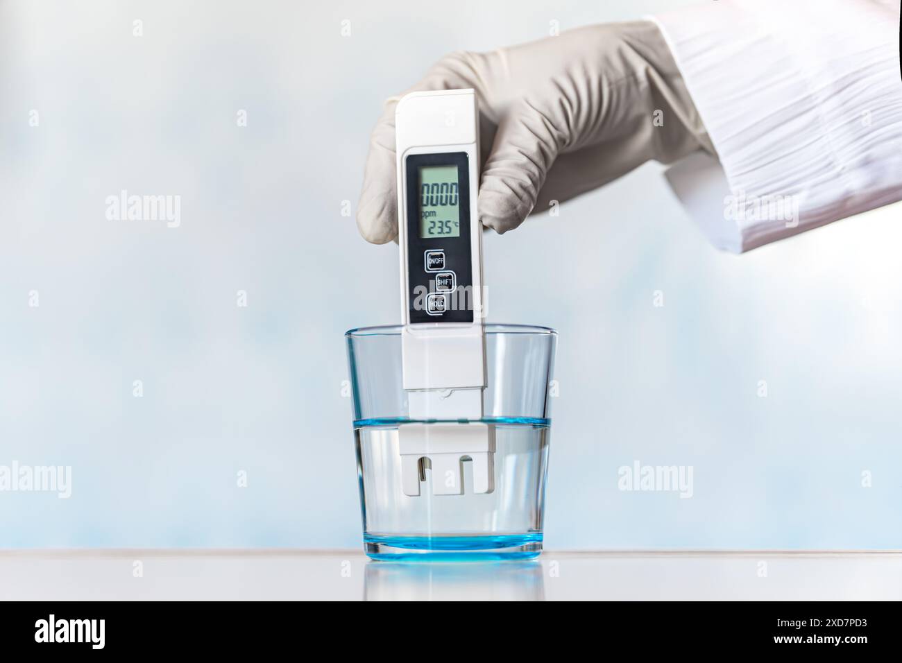 Water quality meter tester submerged in drinking glass, on blue ...