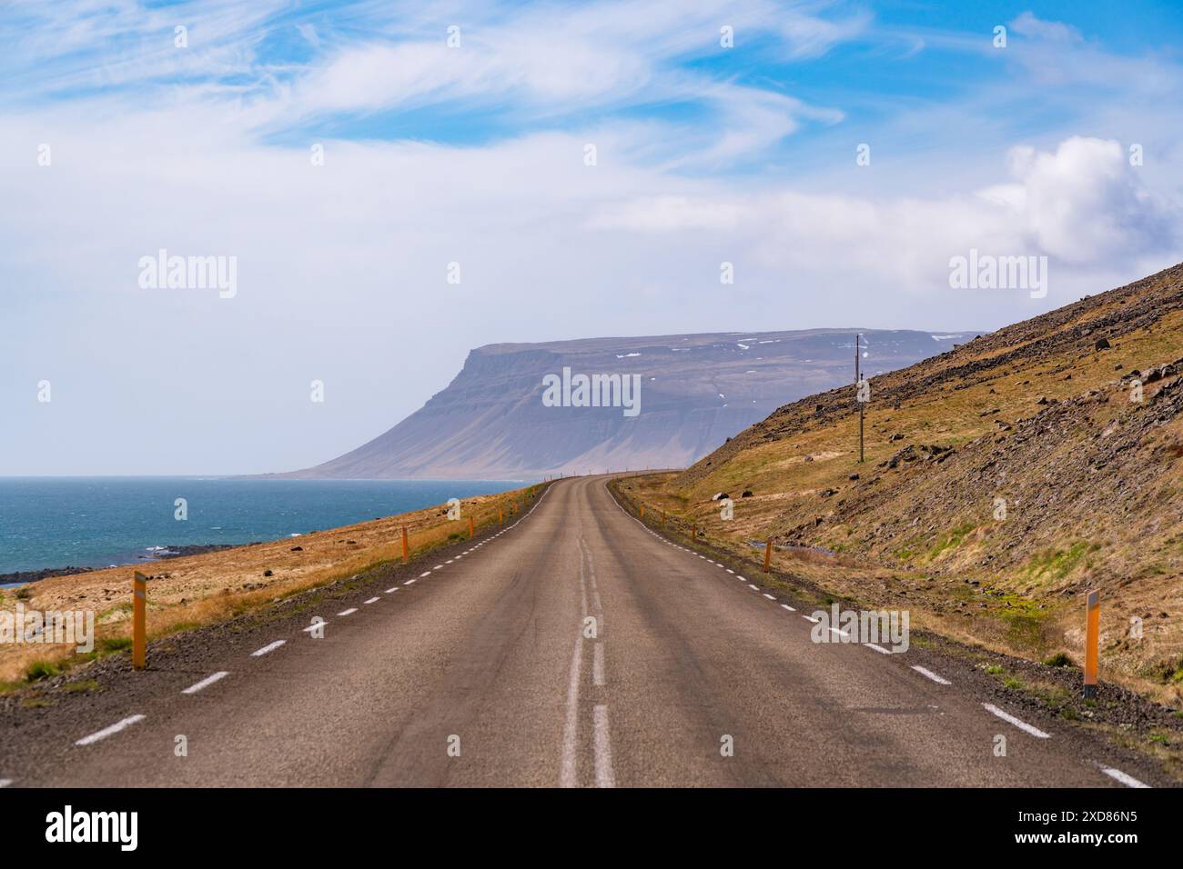 Road in iceland bending around a hill, with high mountains, fjord, sea ...