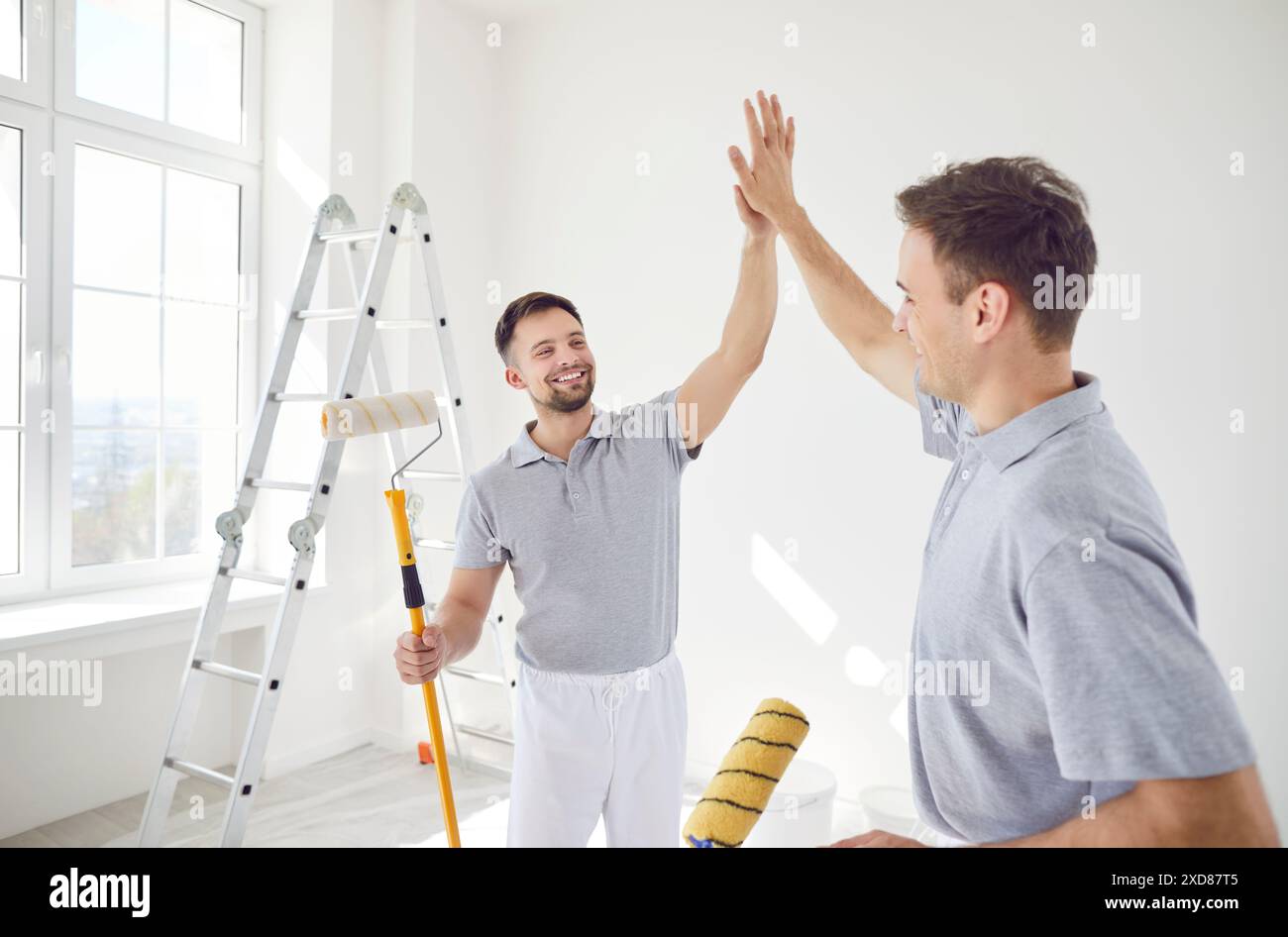 Painters holding paint rollers and giving high five after successful ...