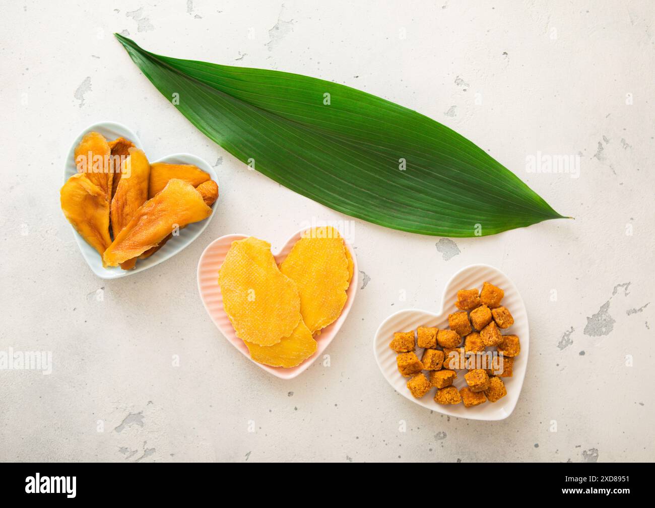 Dried mango slices and balls in heart shaped plates on light background ...