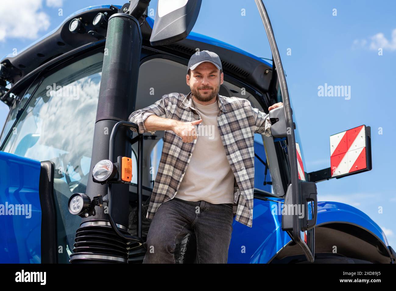 Portrait of a farm worker standing on a tractor and giving a thumbs up ...