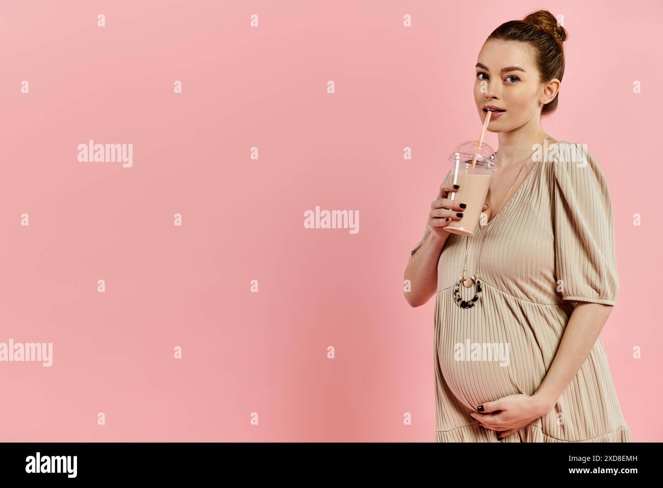 A young pregnant woman in a dress holding milkshake on a pink ...