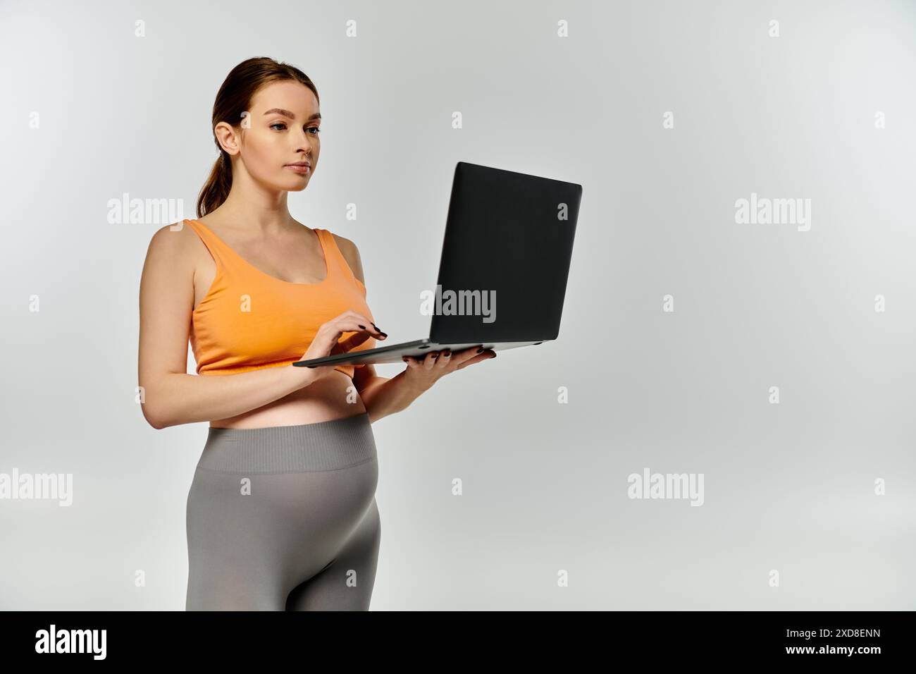 A young, sporty pregnant woman in active wear holds a laptop computer ...
