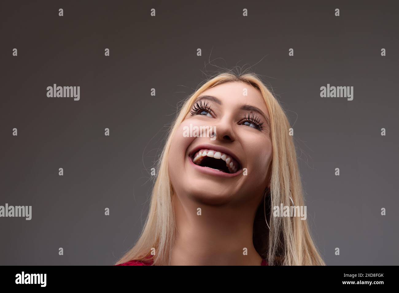 Young woman with long blonde hair is tilting her head back and laughing with her mouth wide open ...