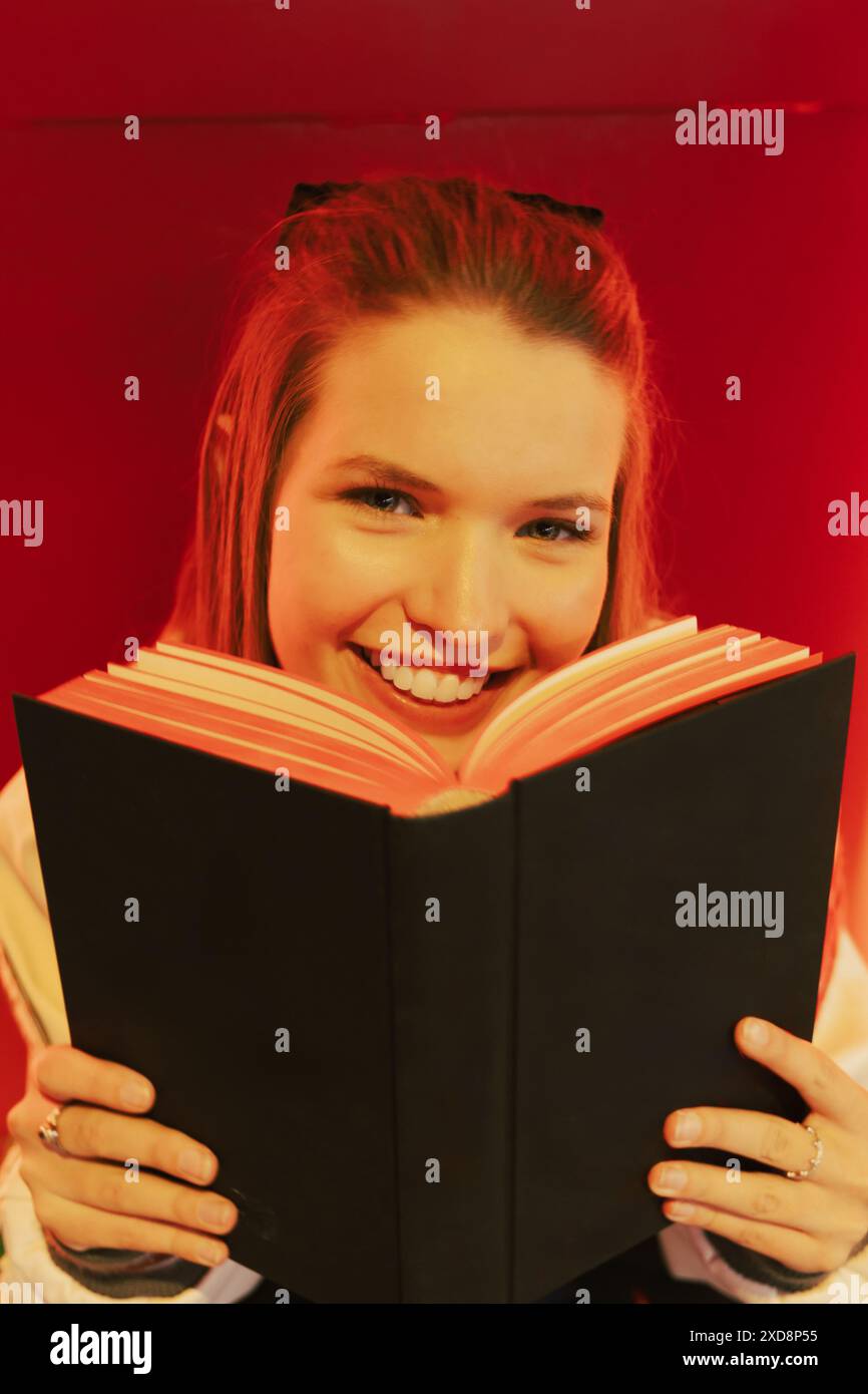 Woman smiling while holding an open book in front of her face, a Stock ...