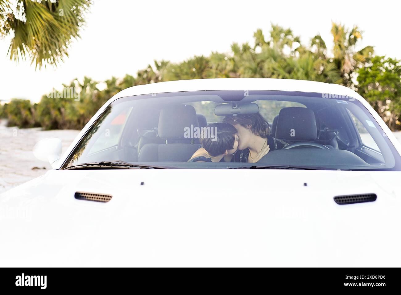 A couple sharing a kiss inside a white car with a tropical backg Stock ...