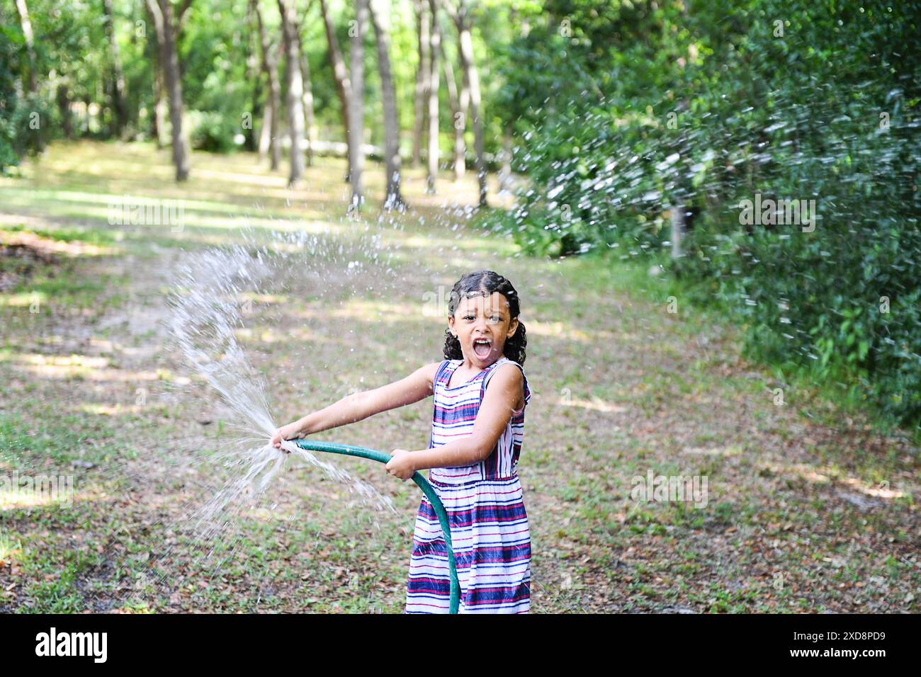 Girl playing with a garden hose, spraying water in a backyard Stock ...