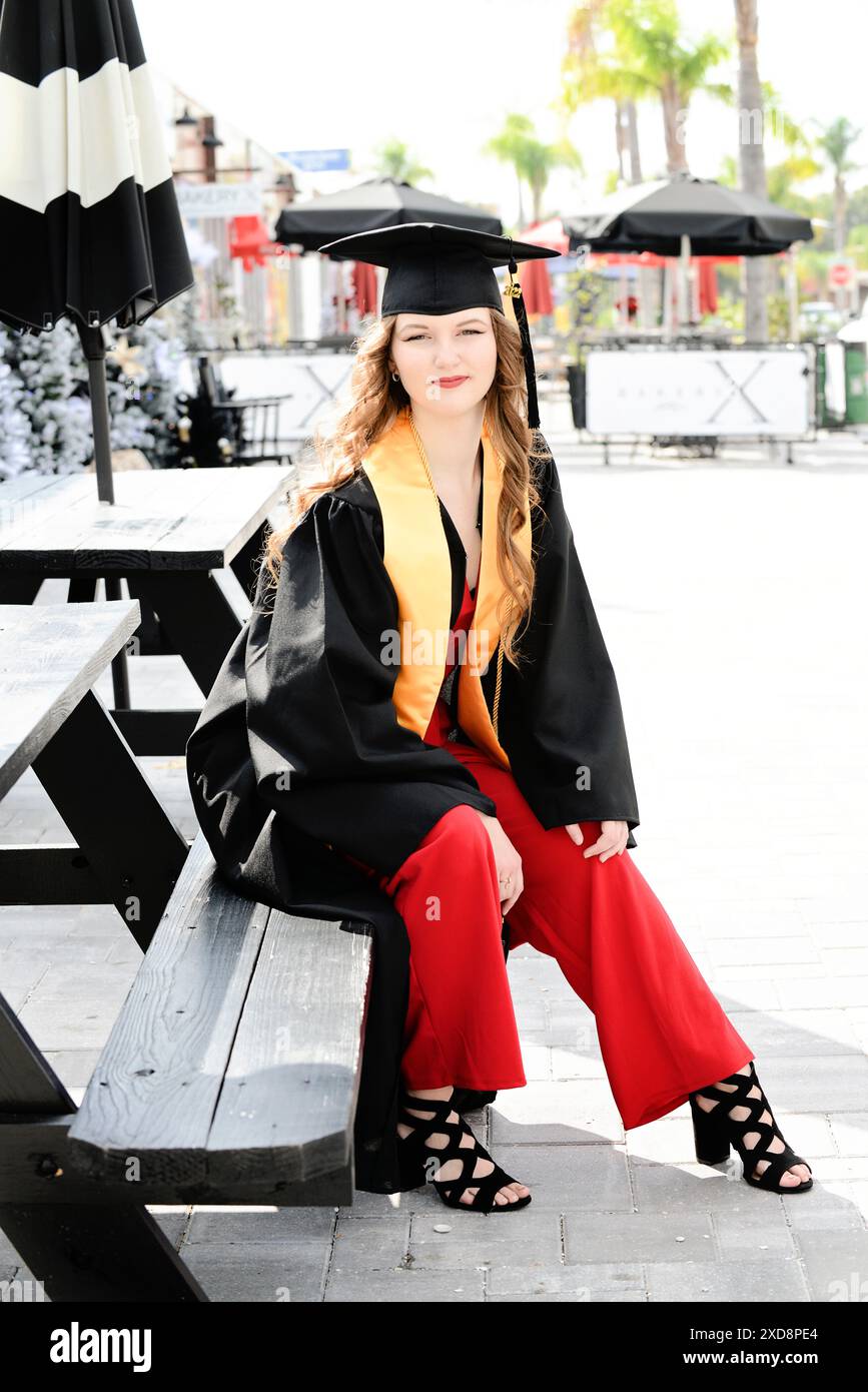 Female graduate in cap and gown, seated on a bench outdoors, loo Stock ...
