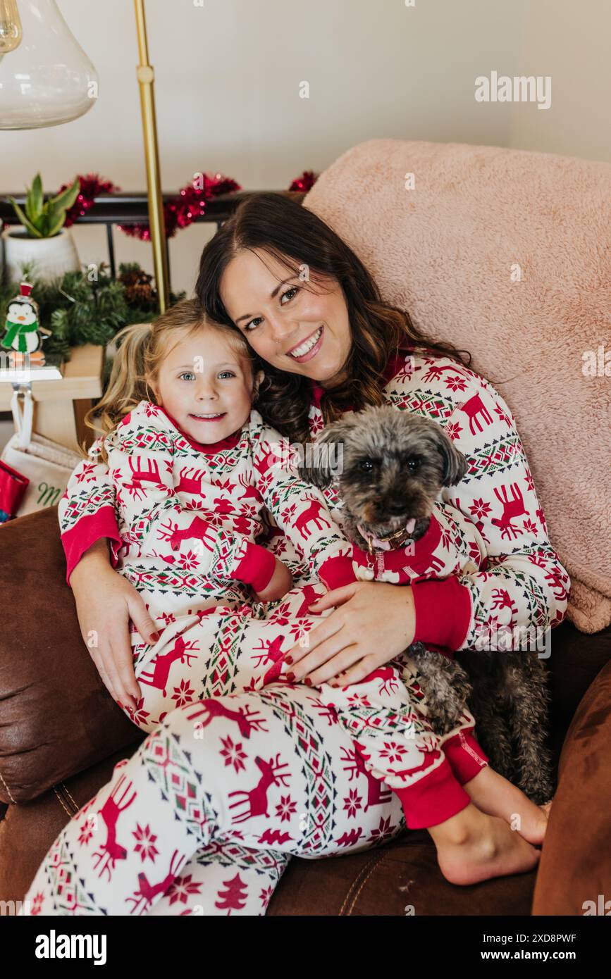Mother and daughter snuggle on living room chair with their dog Stock ...