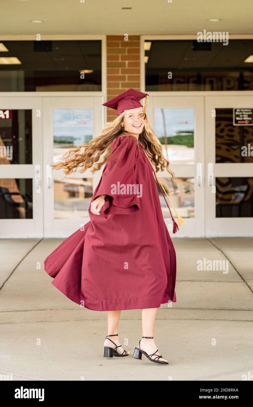 Female graduate spinning in her cap & gown in front of school doors ...