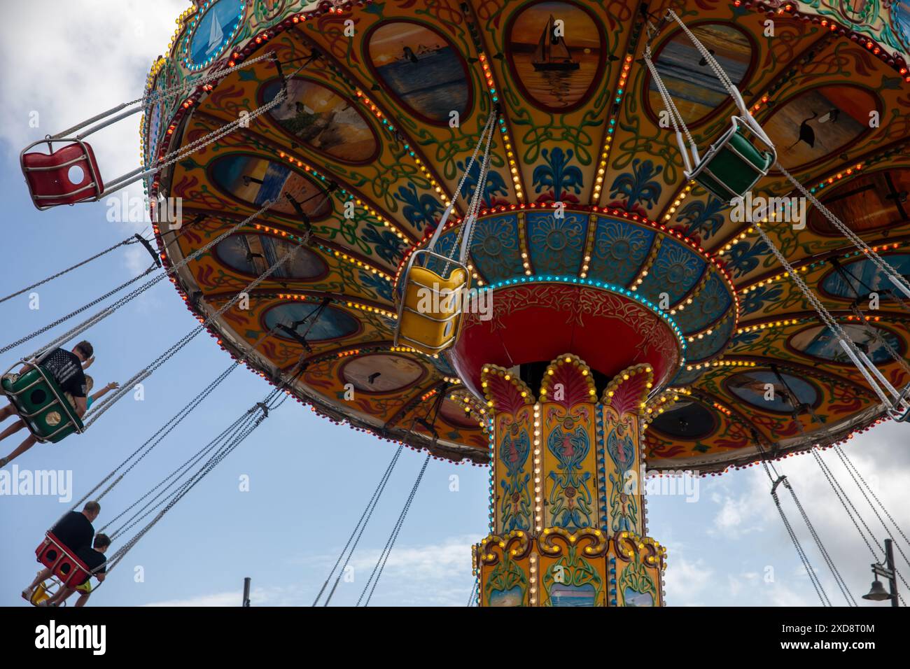 Colorful carousel swing ride with riders in motion against a blue sky ...
