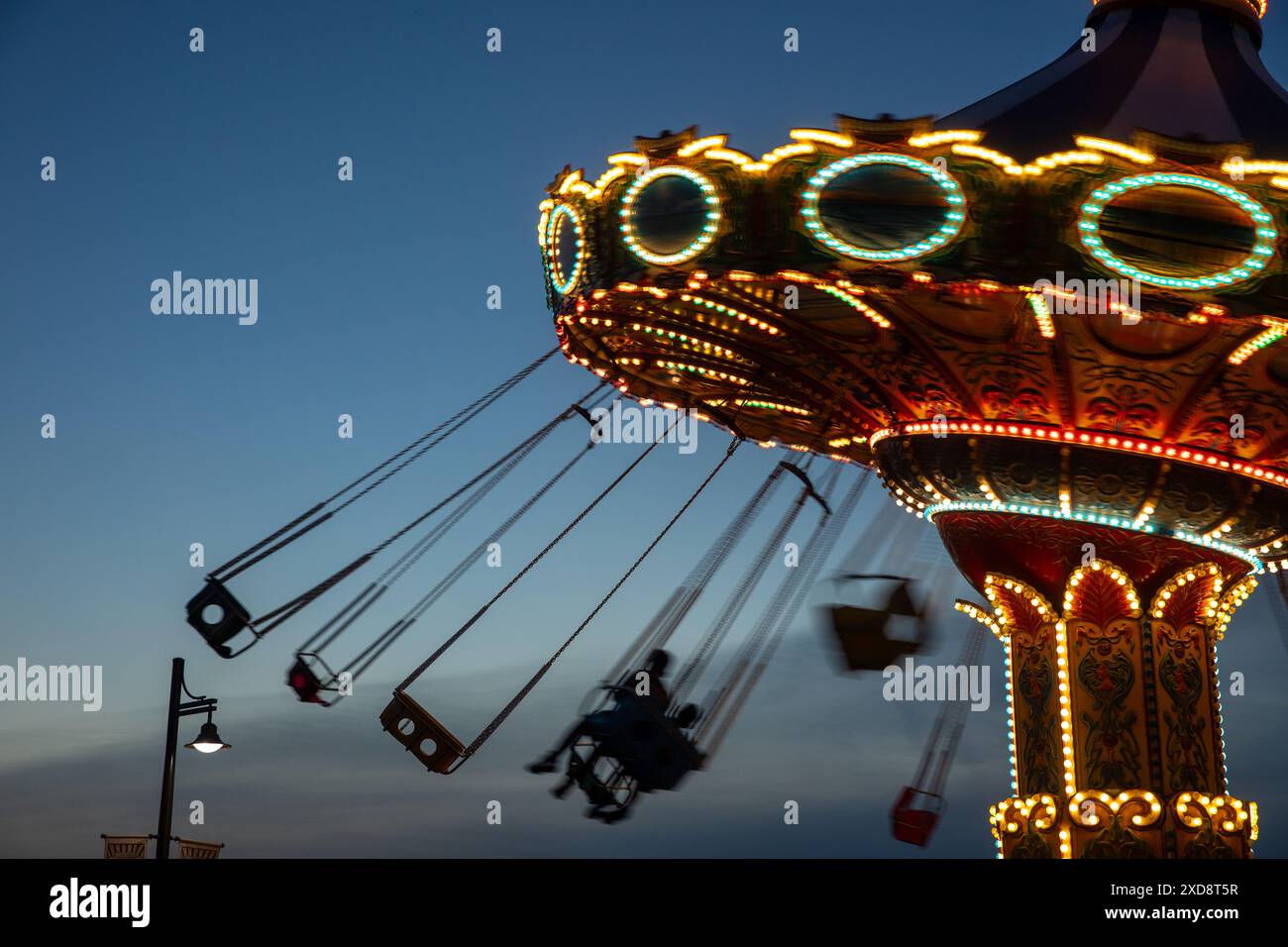 Illuminated carousel swing ride in motion at dusk Stock Photo - Alamy