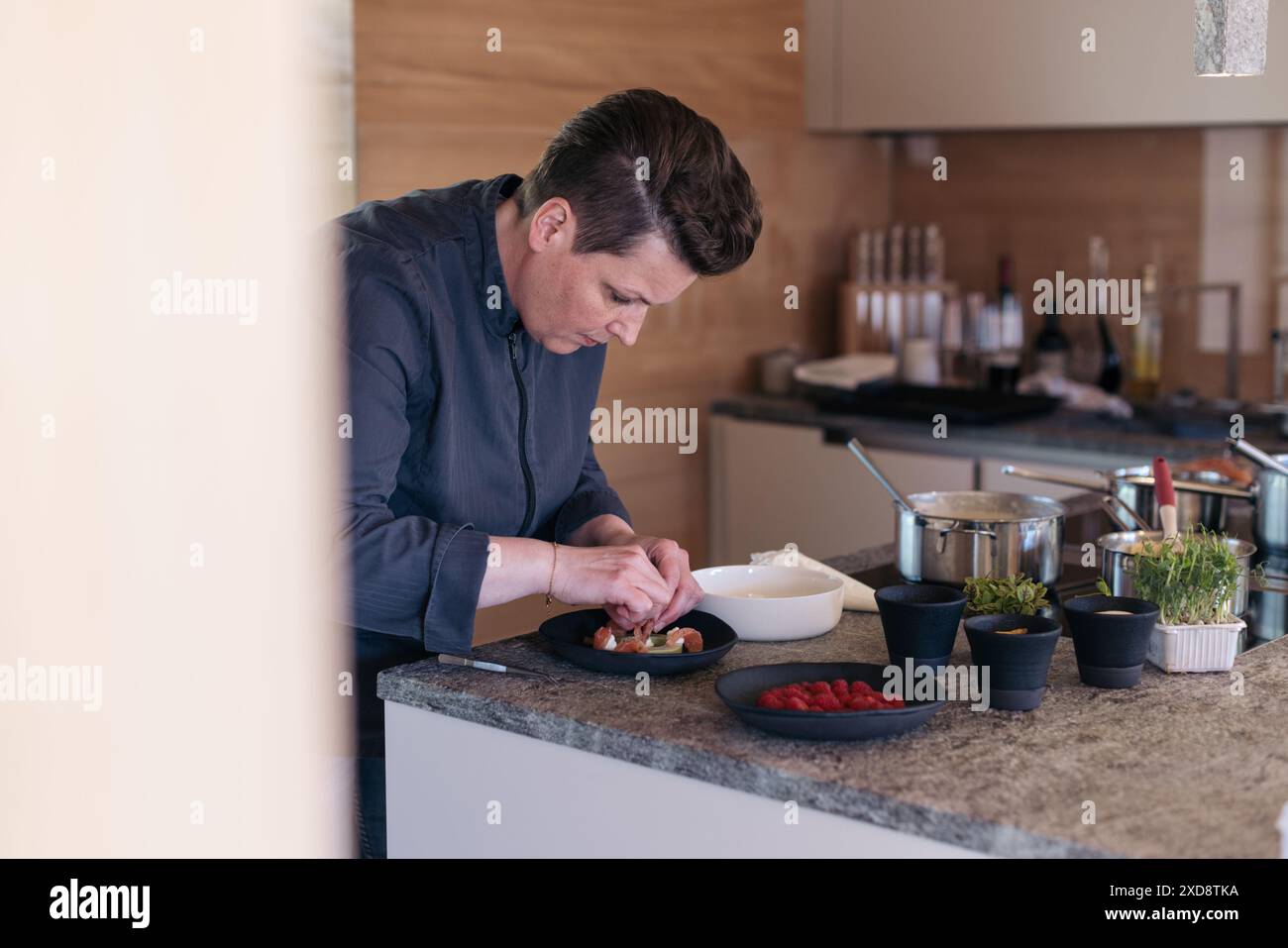 Chef plating food in a modern kitchen with herbs and utensils Stock ...