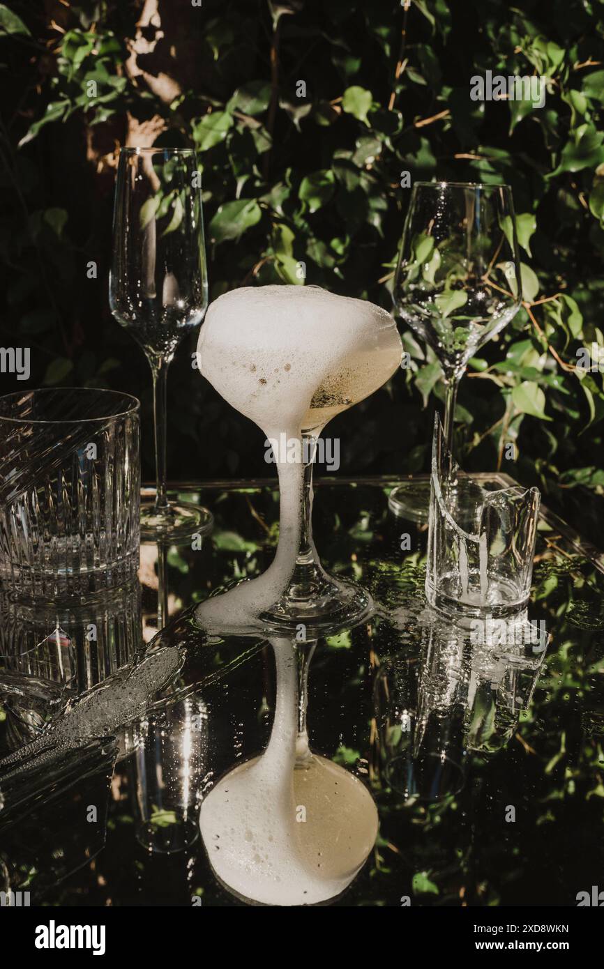 Overflowing champagne glass on a reflective table with empty glasses ...