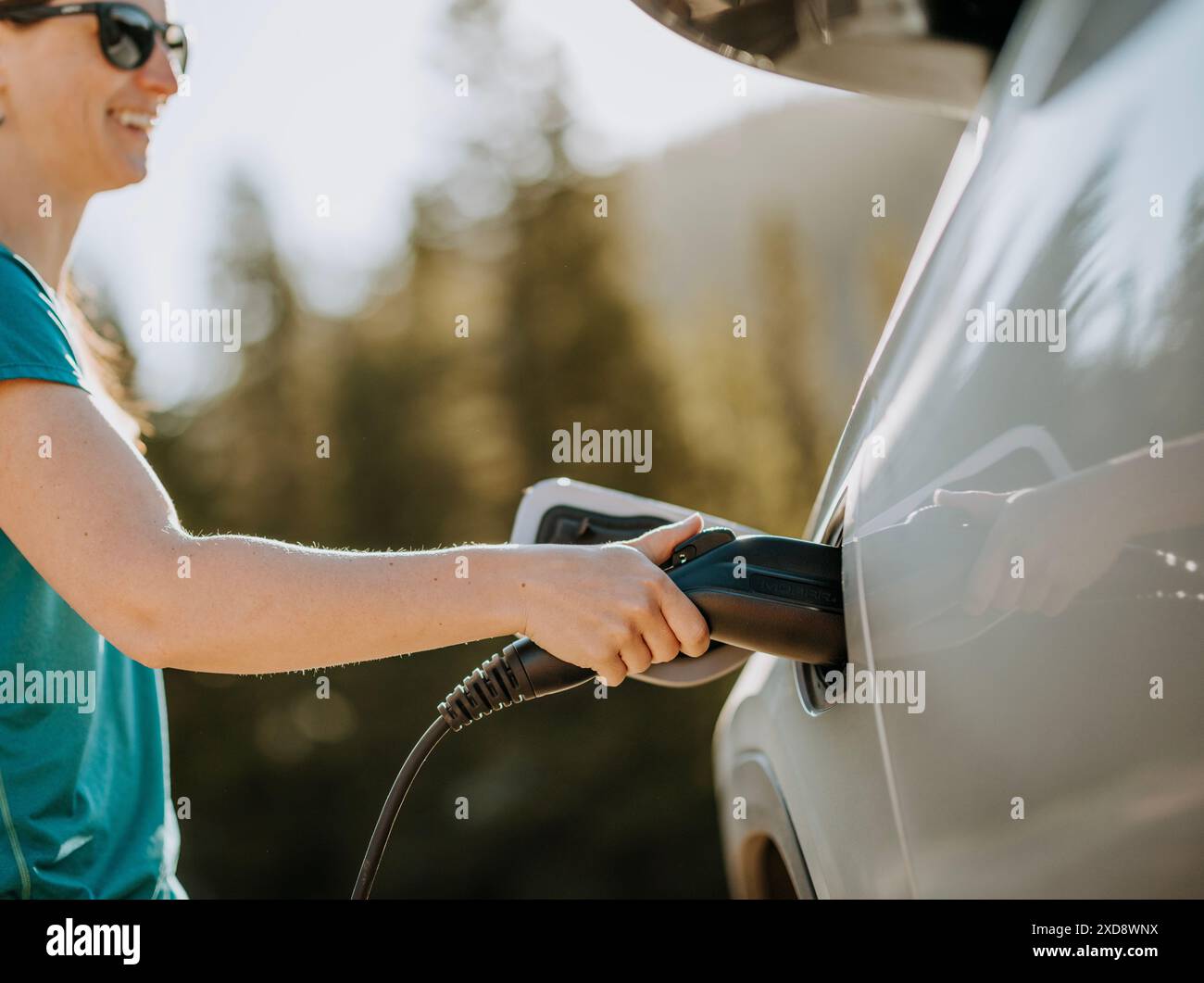 Smiling woman plugs in her hybrid car to charge it's EV battery Stock ...