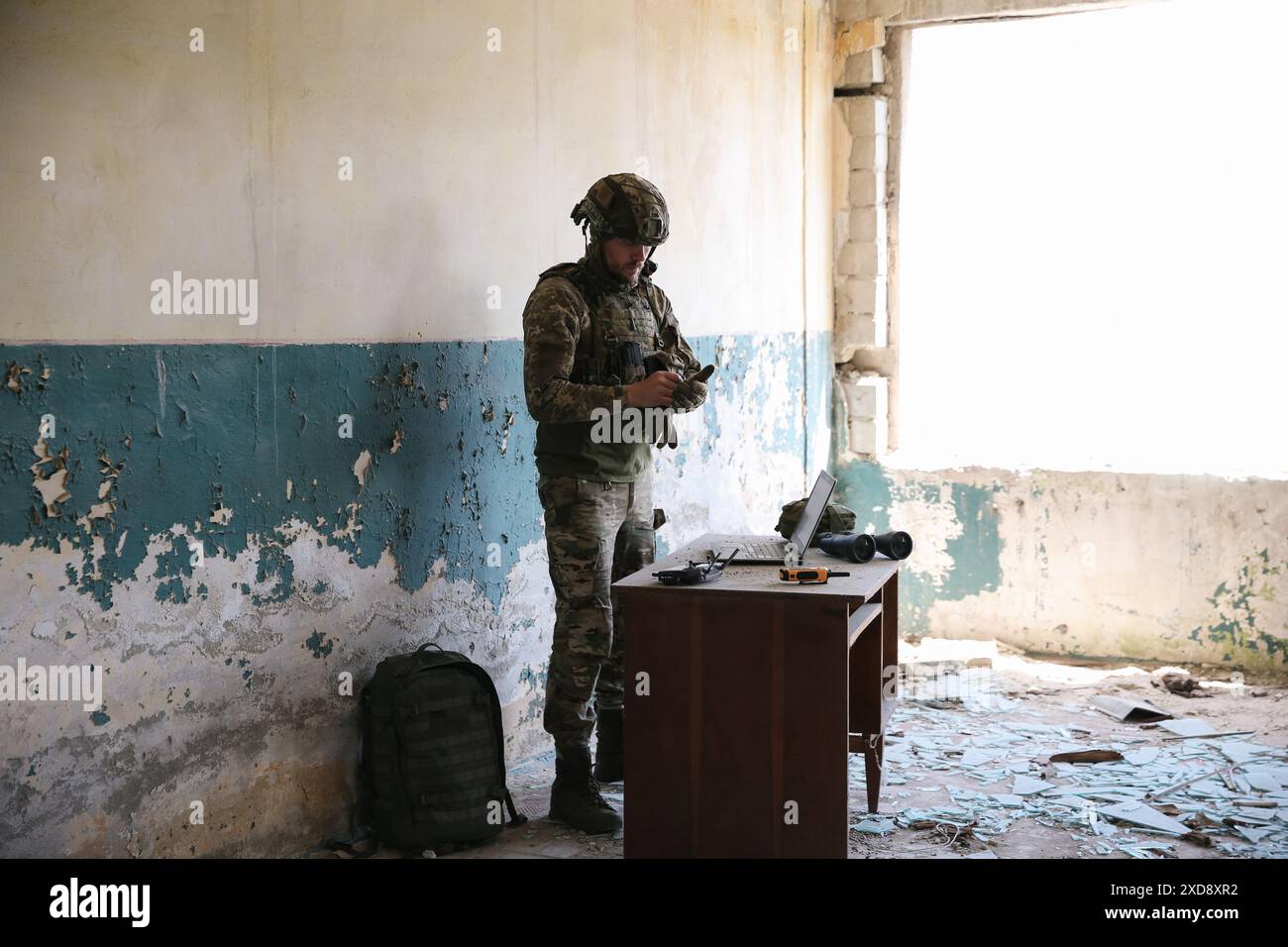 Military mission. Soldier in uniform at table inside abandoned building ...