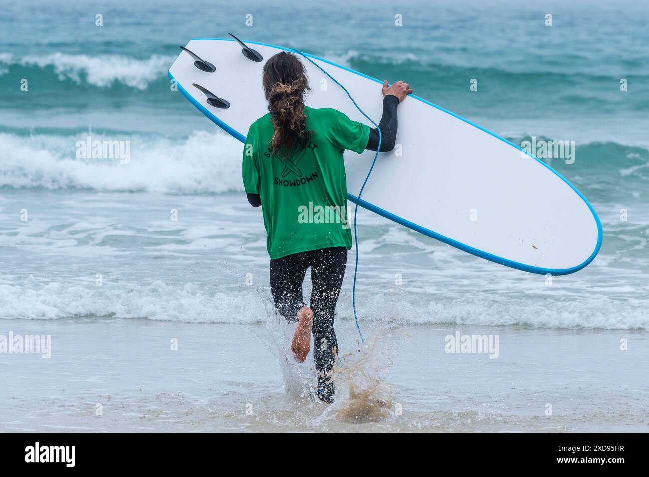 Rear view of an enthusiastic surfer carrying his surfboard and running ...