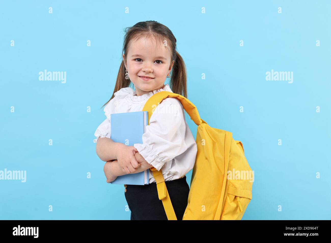 Cute little girl with book and backpack on light blue background Stock ...