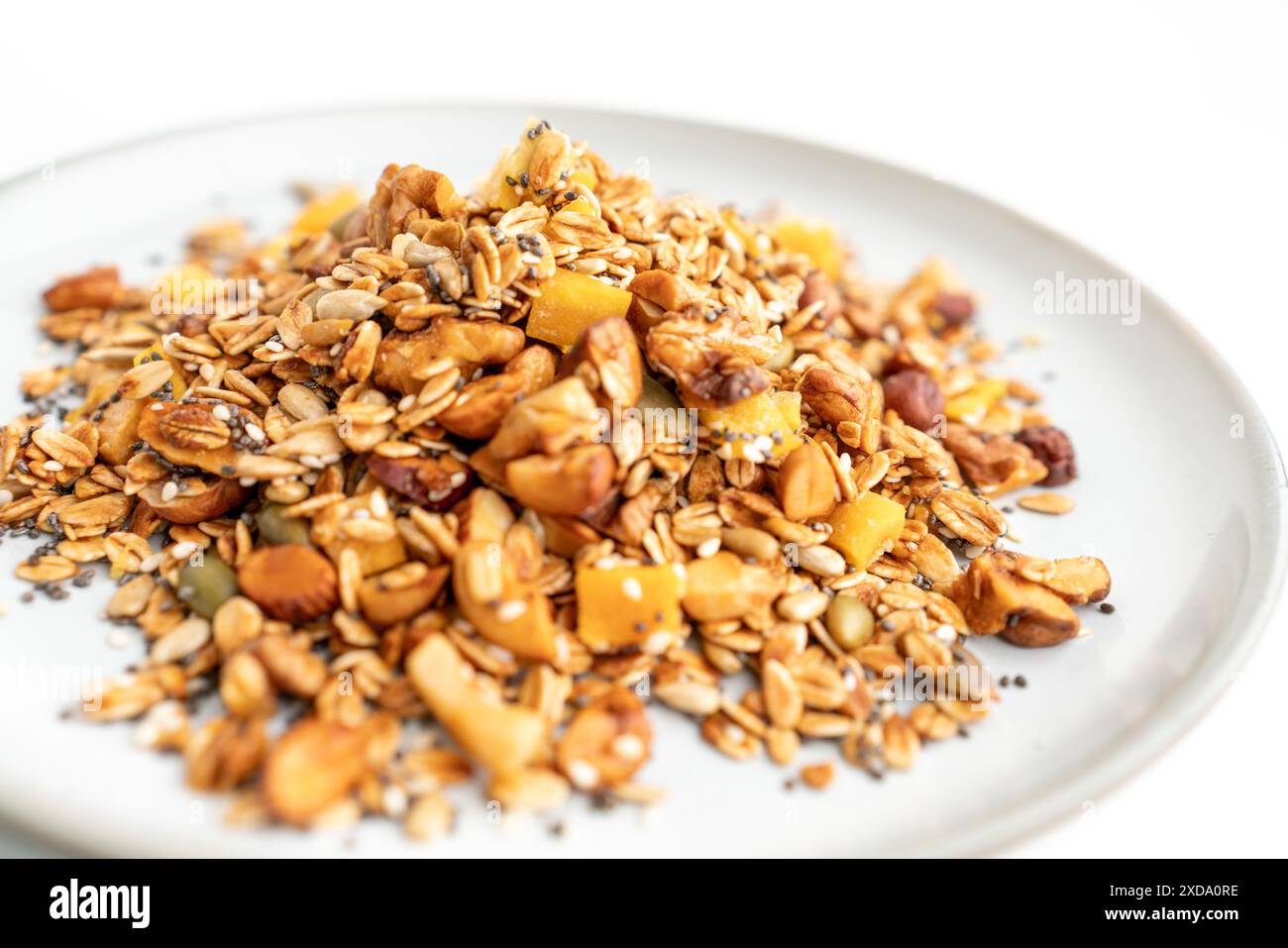 A bowl of granola with nuts and seeds on a white plate. The granola is ...