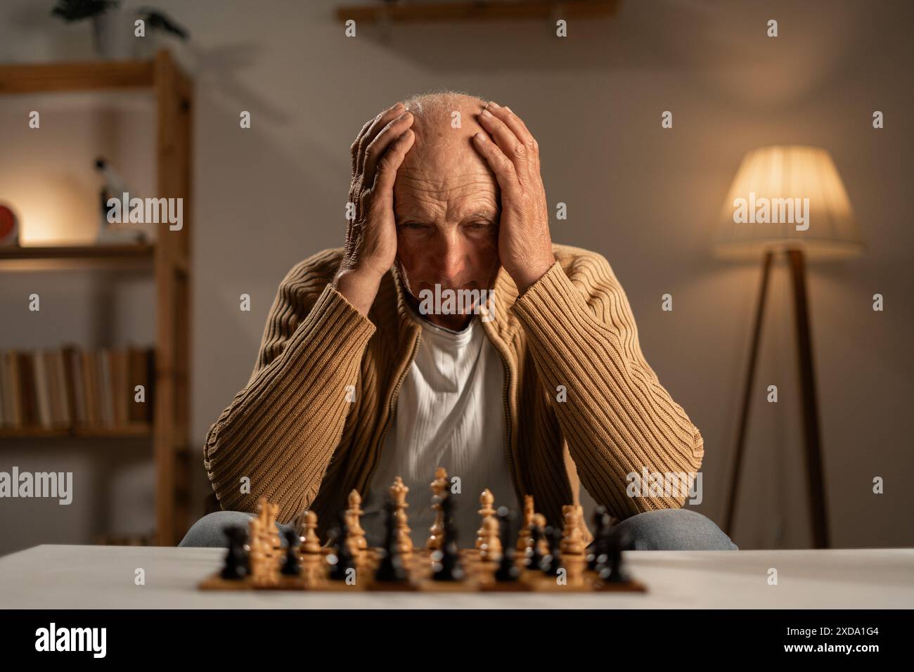 middle aged man playing chess and holding head in hands with sad face ...