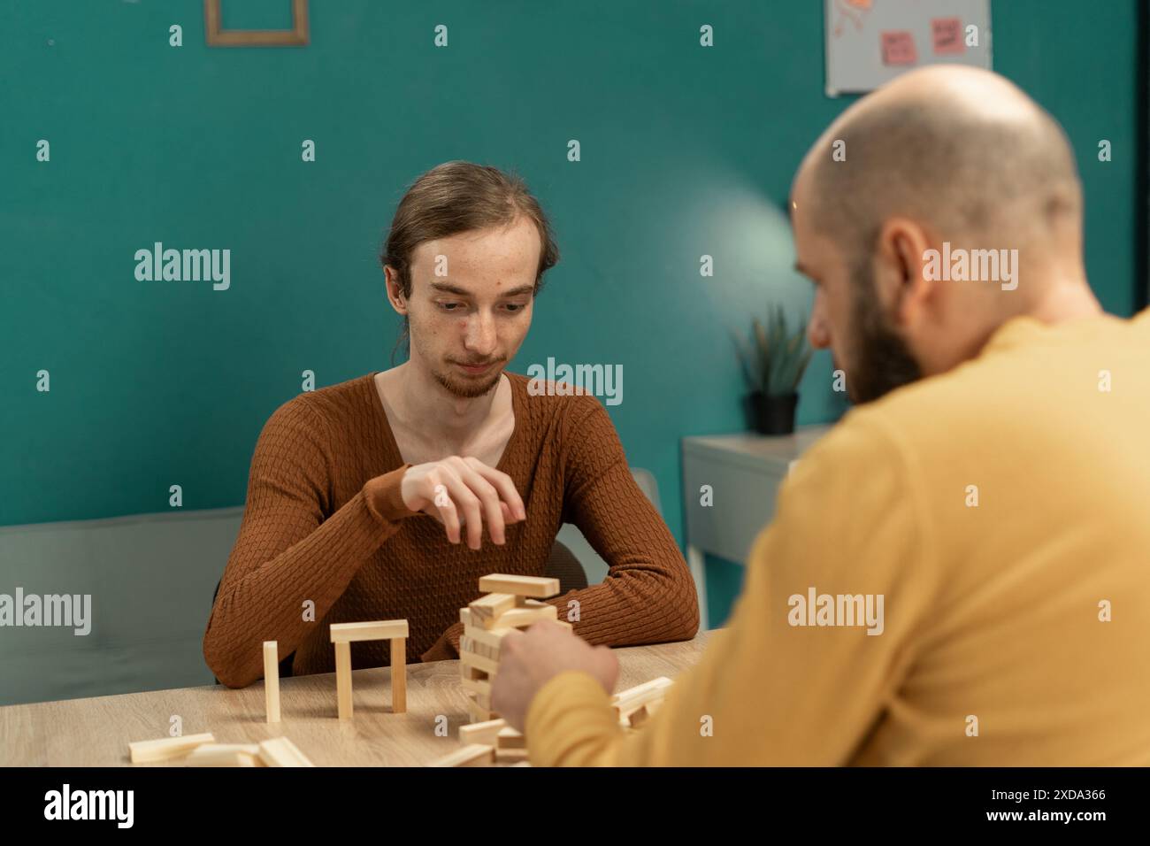 Two men engaged in a tabletop game, stacking wooden blocks to build a ...