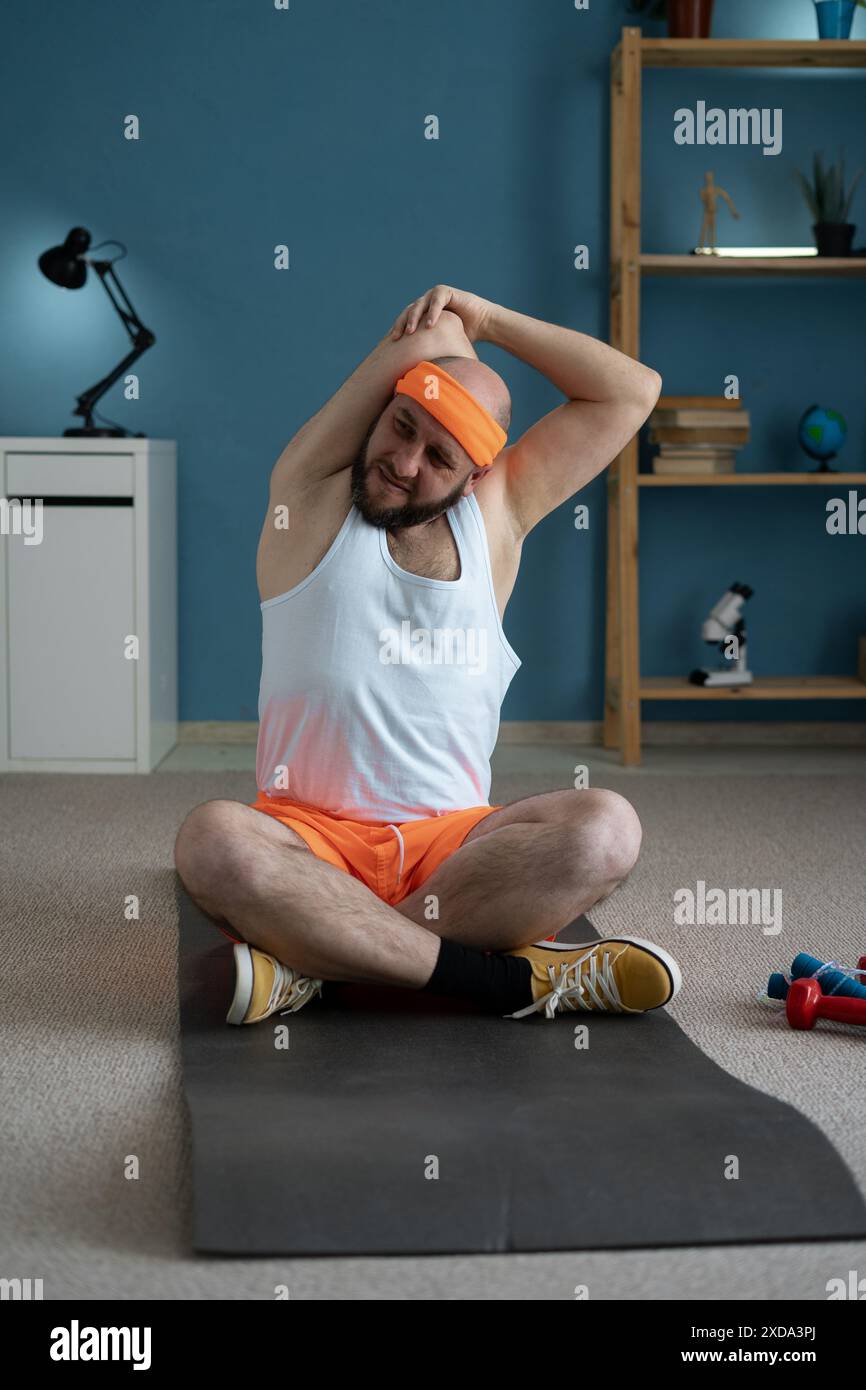 Man stretching triceps while seated on exercise mat at home, focusing ...