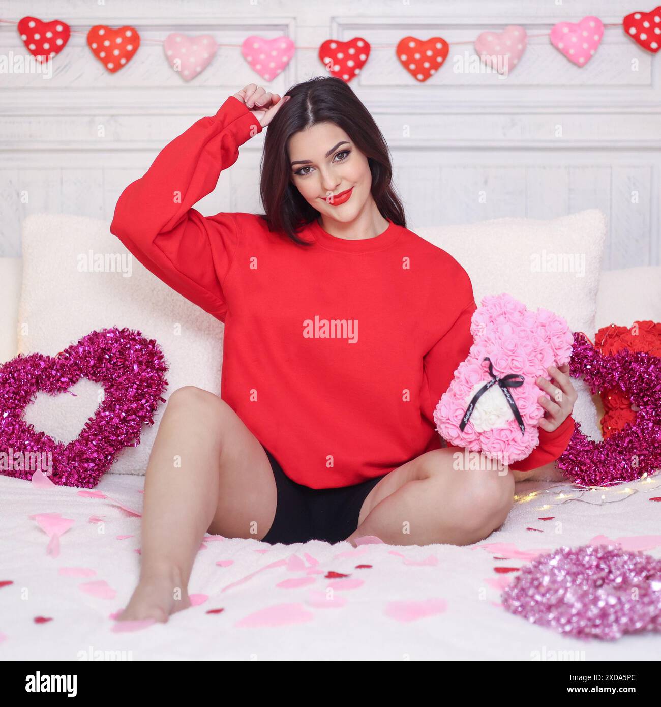Young brunette model on bed decorated for valentines day romantic holiday. Wearing plain top ...
