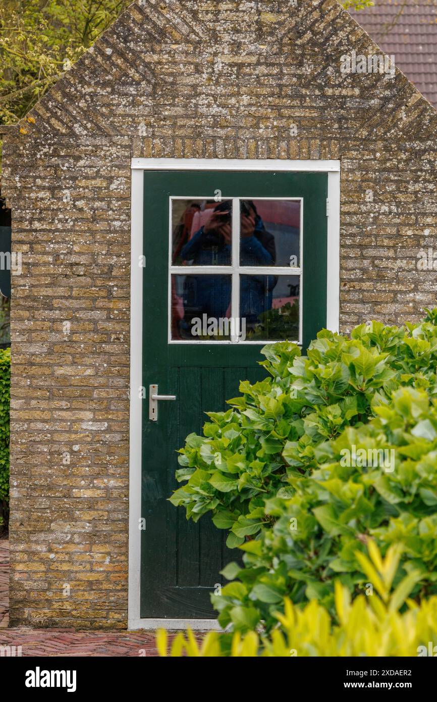 Green door with window in a brick building, in front of it a large bush ...