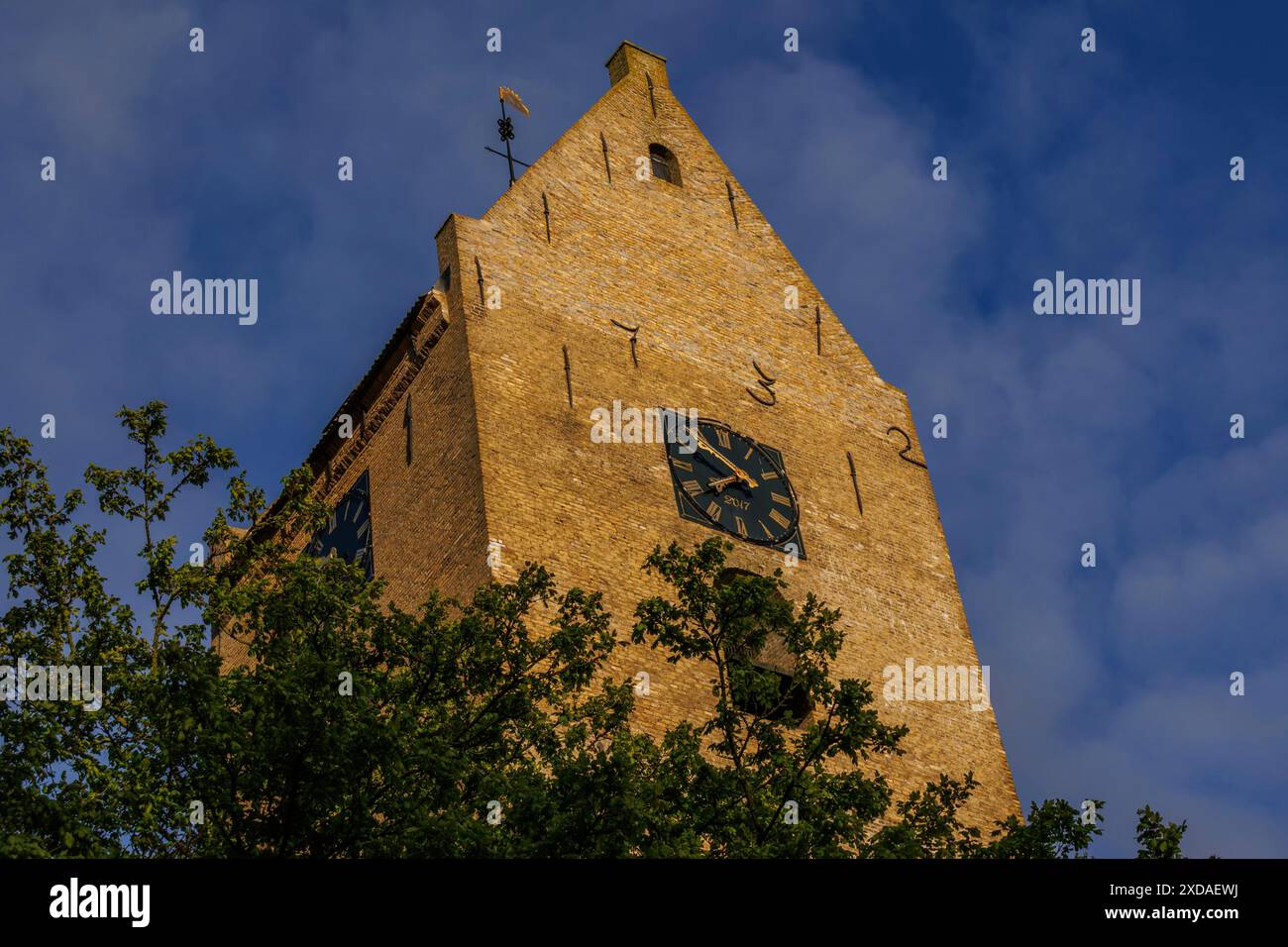 Old brick clock tower in sunlight with a clock on the front and a blue ...