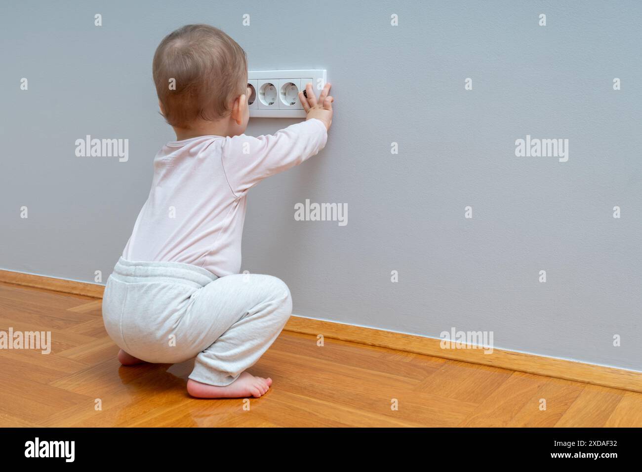 Baby hand reaching for an electrical outlet covered with safety plugs ...
