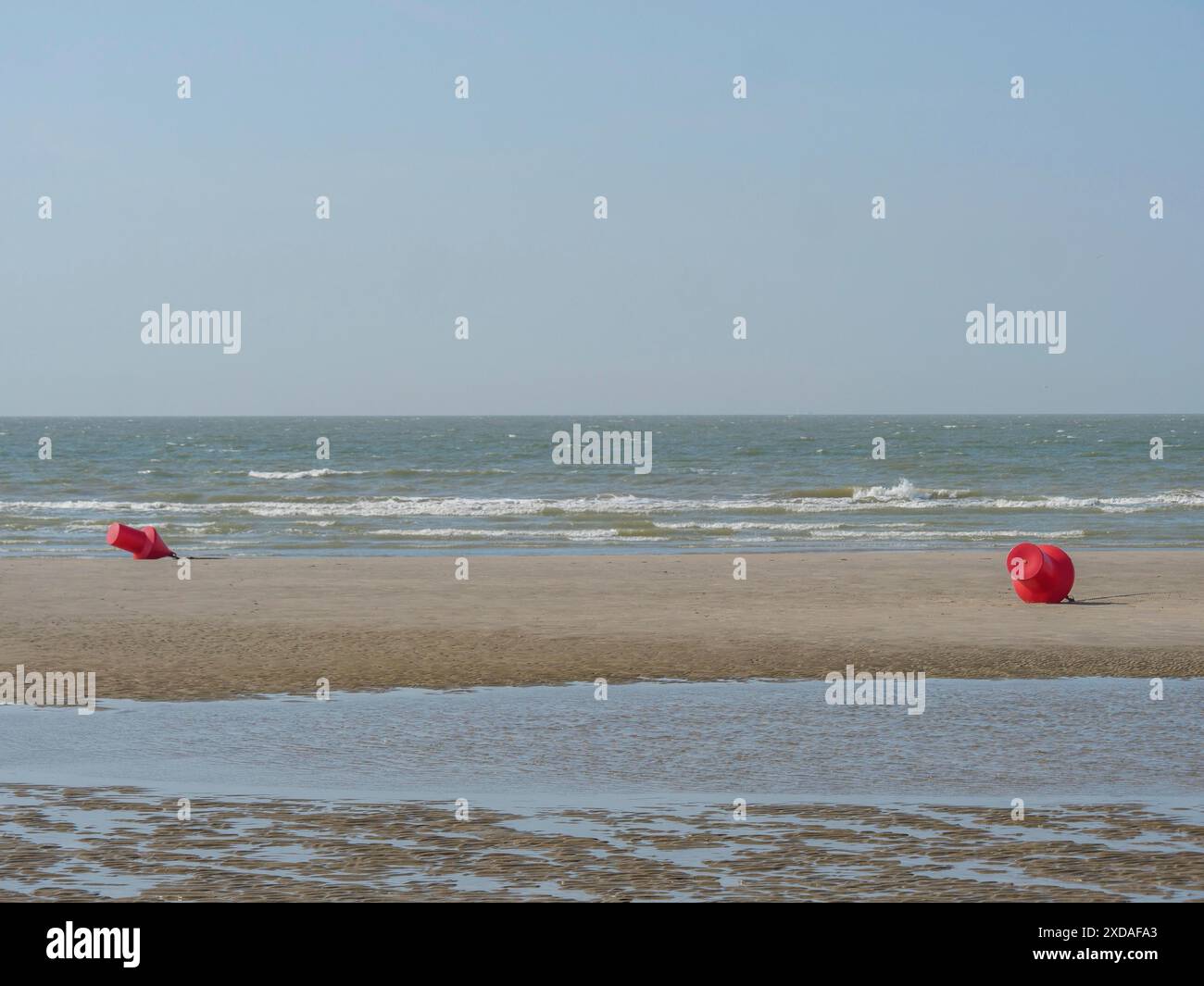 Two red buoys lie on a deserted sandy beach overlooking the sea, de ...